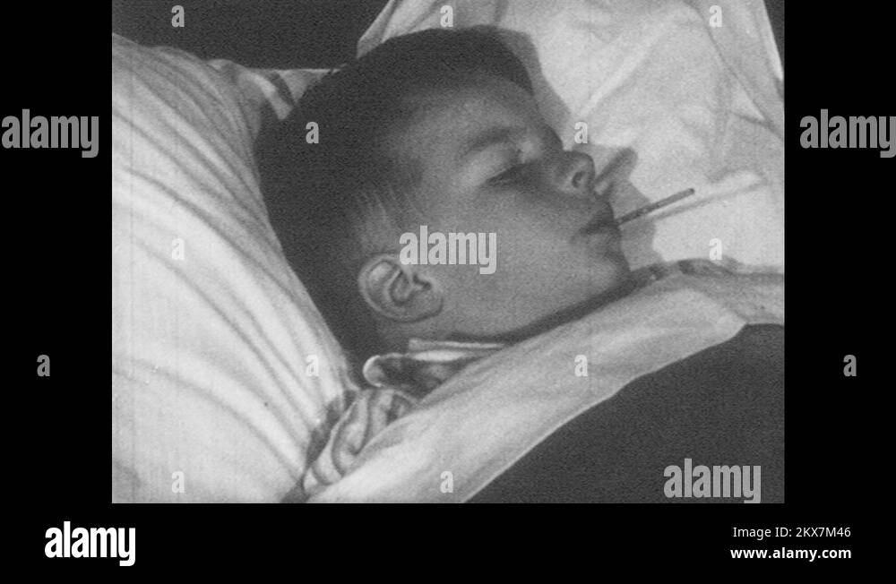 1950s: UNITED STATES: boy sick in bed. Boy with fever. Thermometer in ...