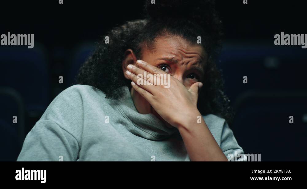 A terrified woman covers her face as she struggles to watch a scary ...