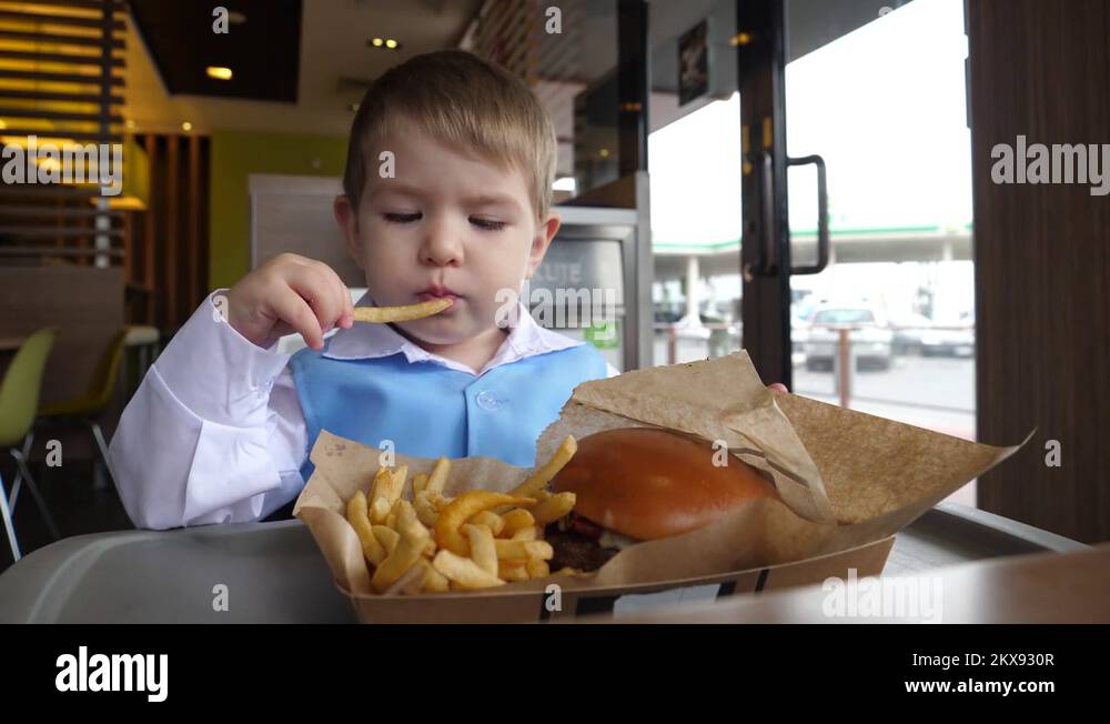 Child boy portrait eating chewing french fries potatoes in fast food ...