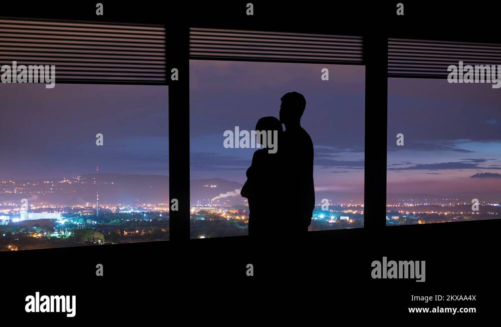 The man and woman hug near the window on a night city background. time ...