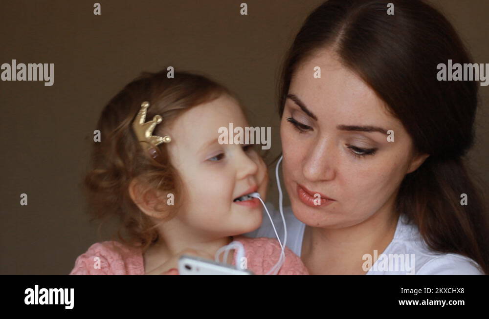Mother and daughter in headphones look at the screen of the smartphone ...