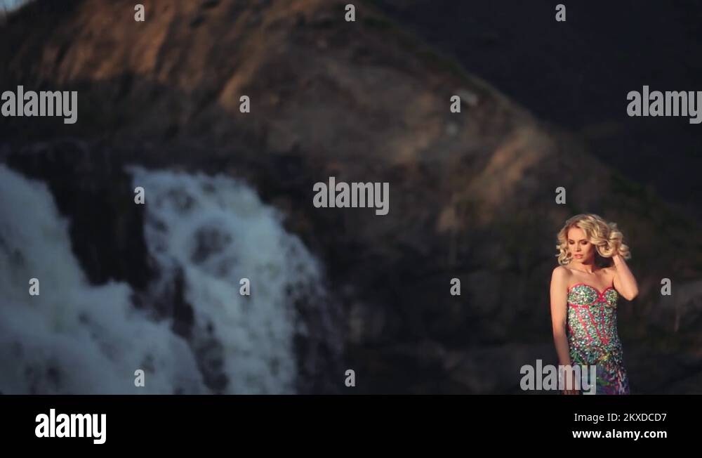 Beautiful Sexy Girl In A Dress Posing Against A Waterfall Background