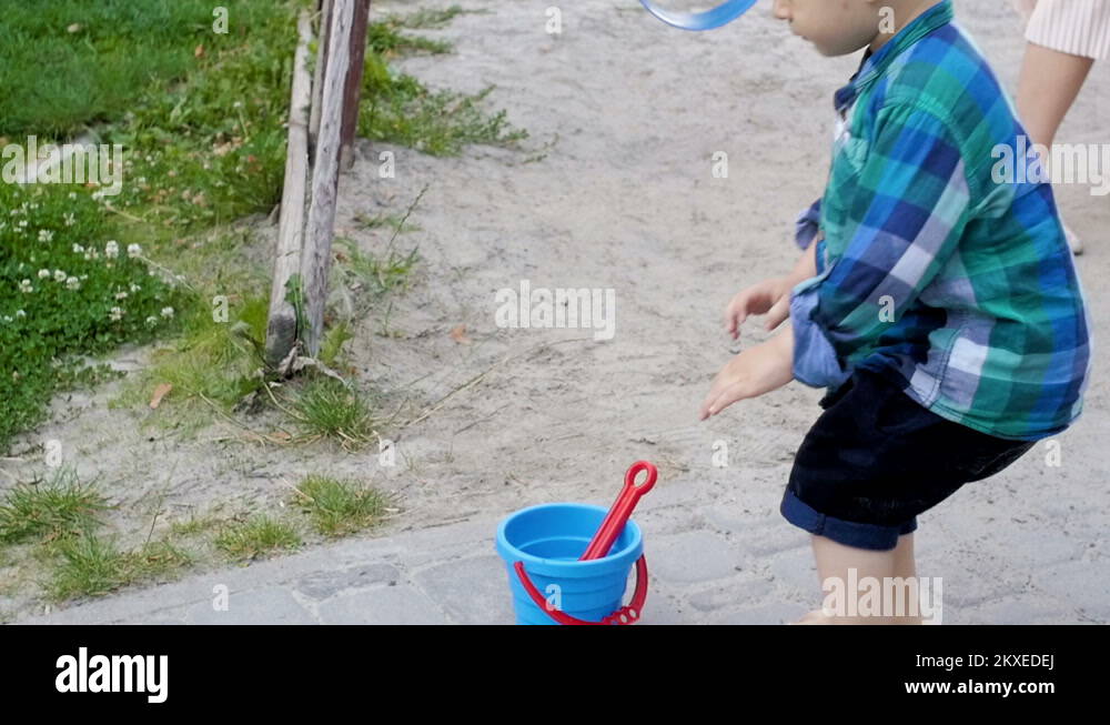 Slow motion footage of barefoot toddler boy carrying plastic bucket and ...
