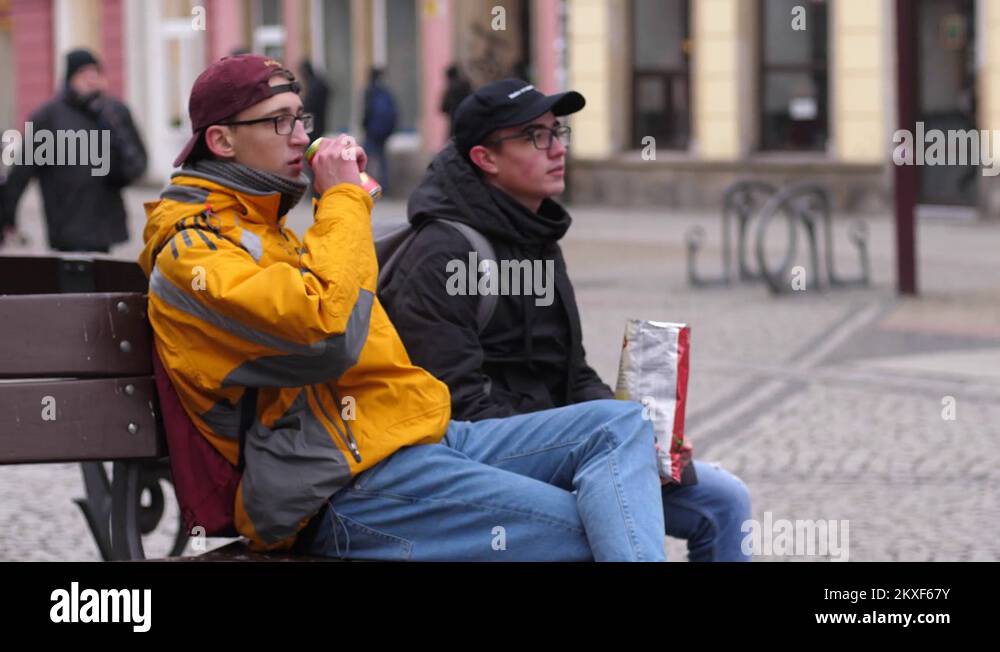 Friends teenagers sit on bench eat chips and drink cola from a can in ...