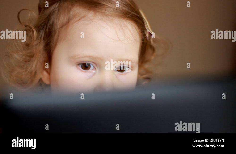 A little cute girl looks at the screen monitor computer or laptop ...