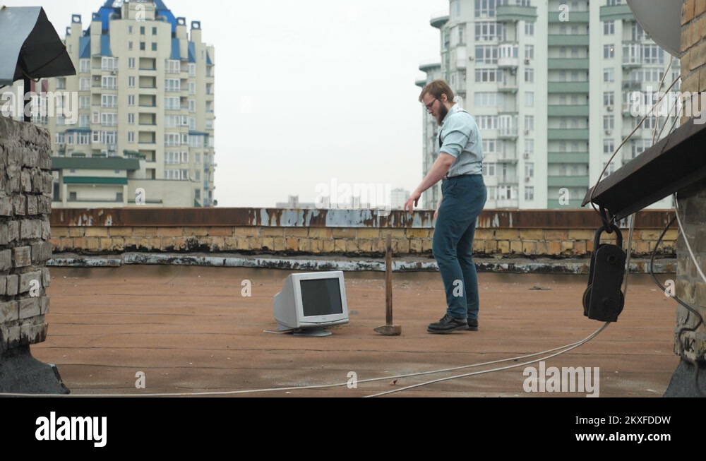 Young strong man smashes the monitor with a sledgehammer on the roof ...