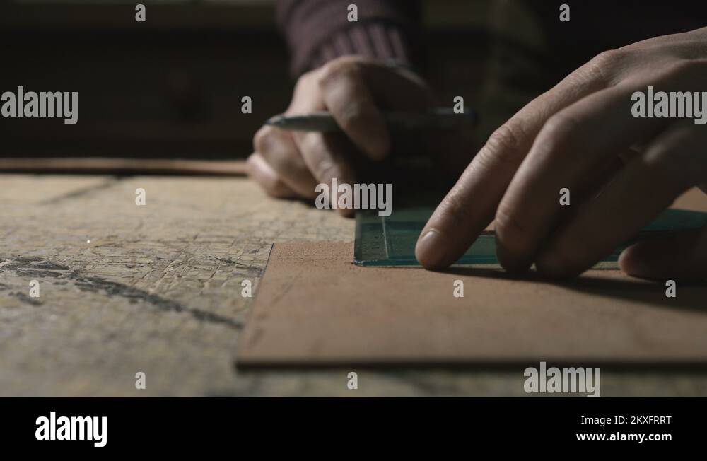 Leather craftsman drawing a cutting line using a pen and a bracket ...