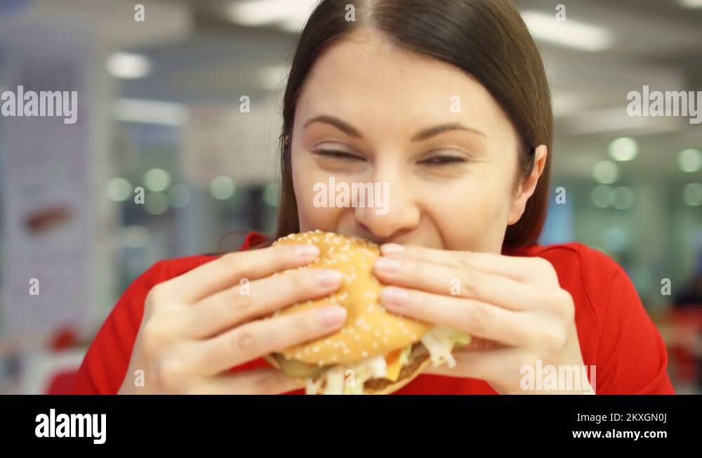 Very hungry girl eating hamburger on food court. Woman biting ...