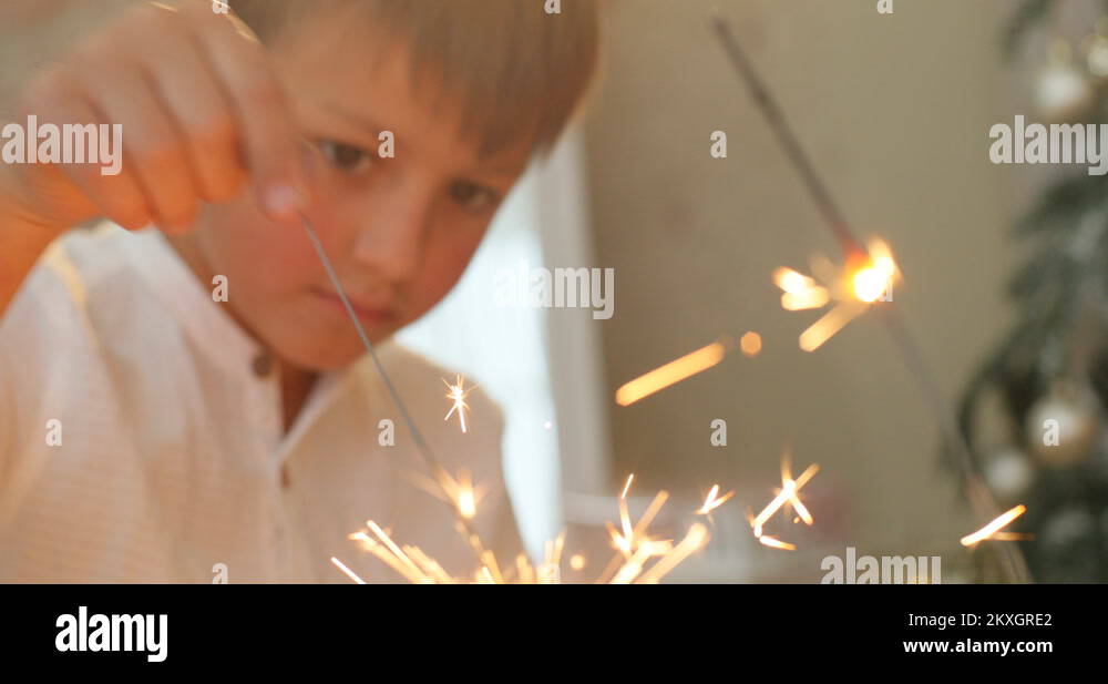 Close-up portrait of child boy holds lighted fireworks in the glitter ...