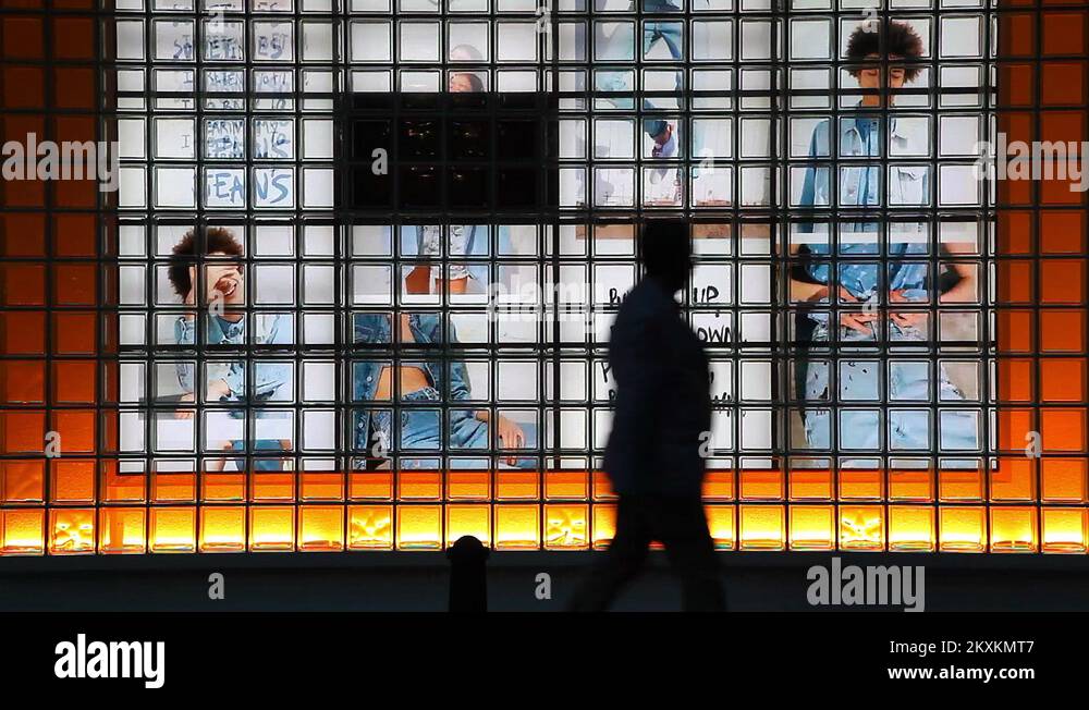 Silhouettes of people passing digital fashion window display in ...