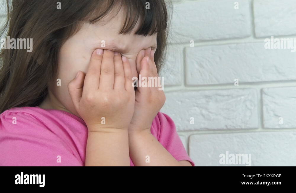 The child is crying. The sad little girl covered her face with her ...