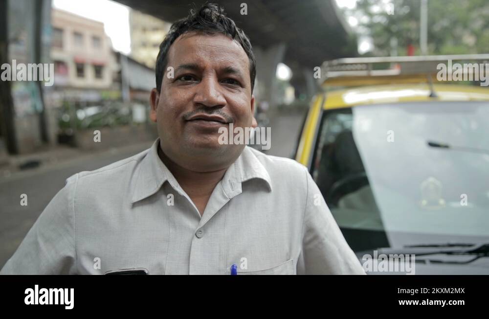 A confident and smiling Indian taxi driver standing along the road ...