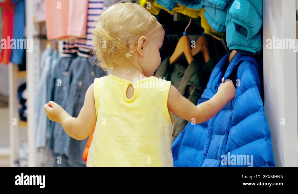 Little girl touching clothes in childrens clothing store during family ...