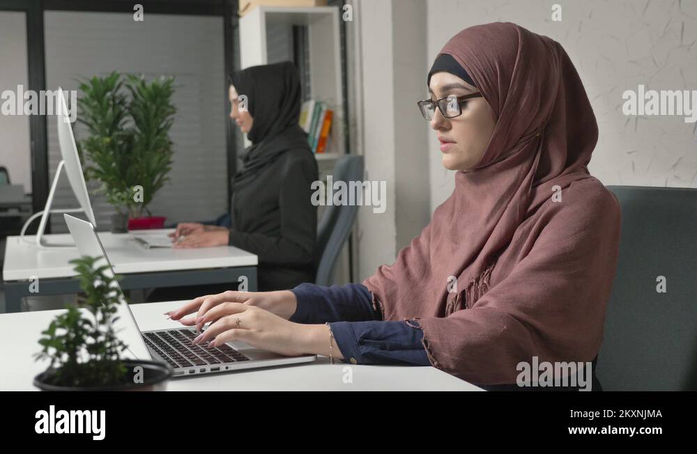 Two young beautiful Arab girls in hijabs work in the office, typing. 60 ...