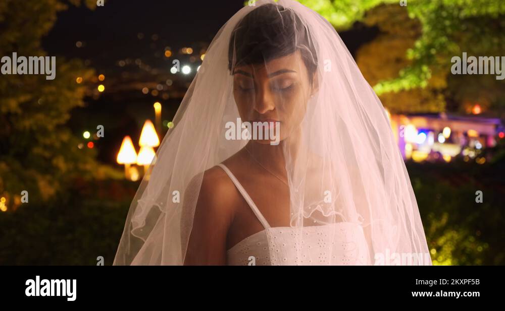 Blushing bride in wedding dress and veil poses for portrait at night ...