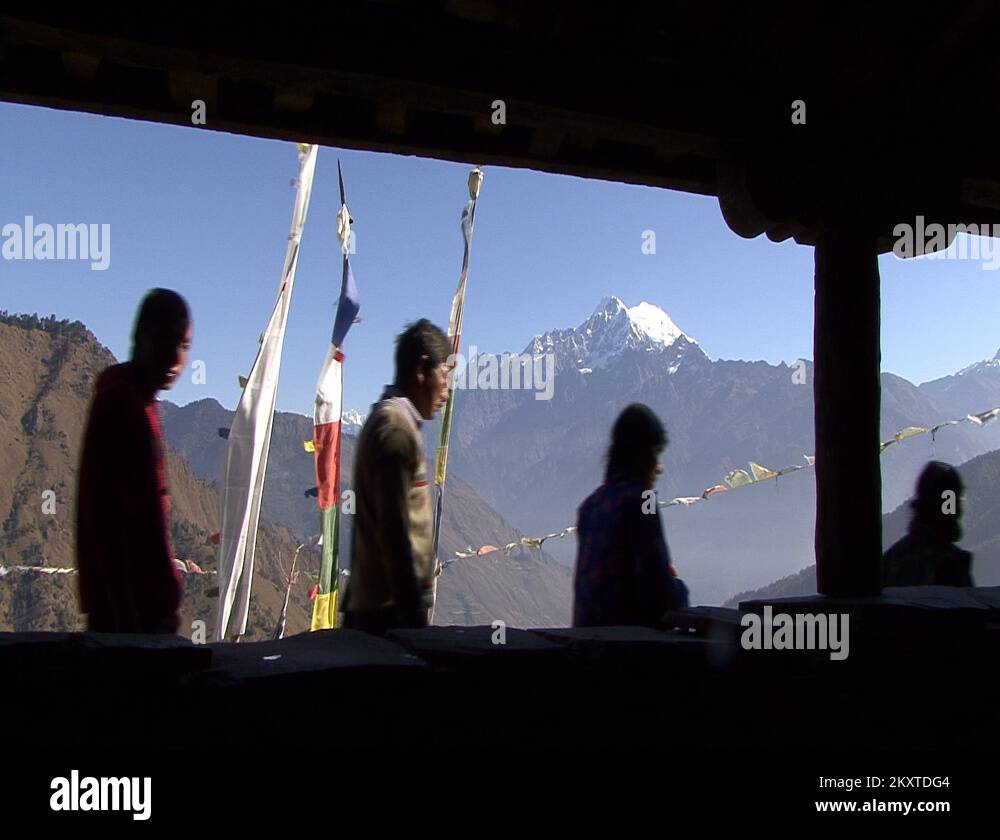 Villagers walk past prayer flags with Himalayas in background Stock ...
