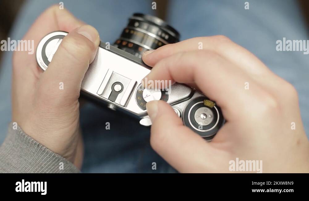 A young photographer changes shutter speed of a vintage old film camera ...
