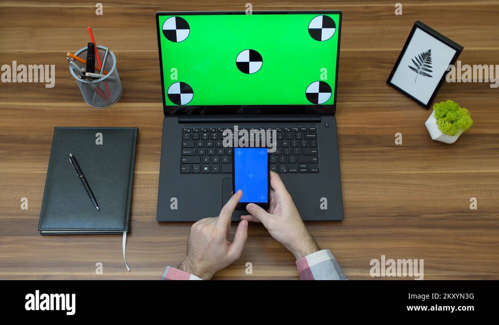 Man's taping on the smartphone with blue screen and a laptop with green ...
