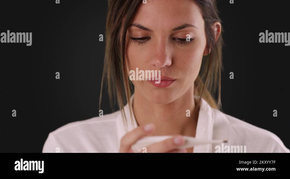 Sick girl with fever checking temperature with thermometer on dark gray ...