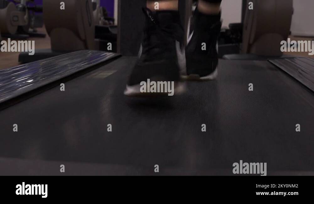 A fit woman runs on a treadmill in a gym - front closeup on the feet ...