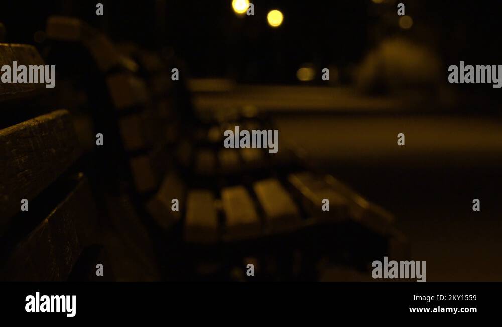 A row of benches in a dimly lit alley in the night - closeup - a jogger ...