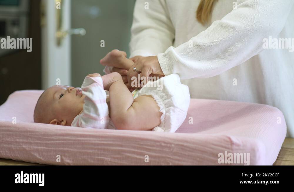 Mother changing baby daughter's nappy, panning left, surface level ...