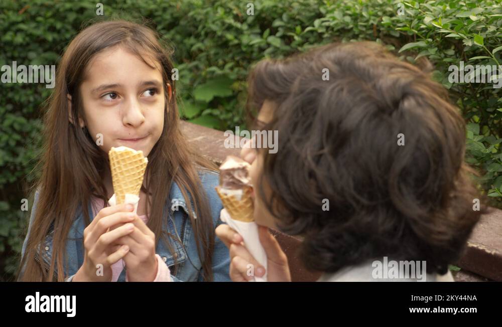cute teenagers, boy and girl eating ice cream in the park and talking ...