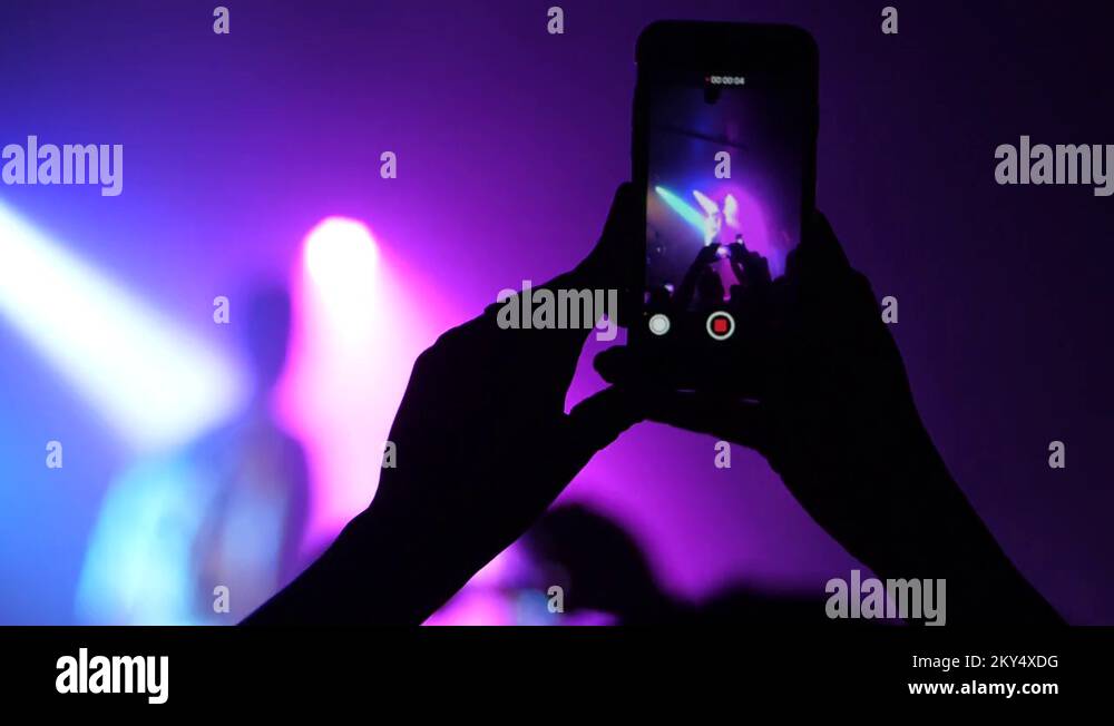 Mobile phone shooting a music concert by spectator silhouette hands ...