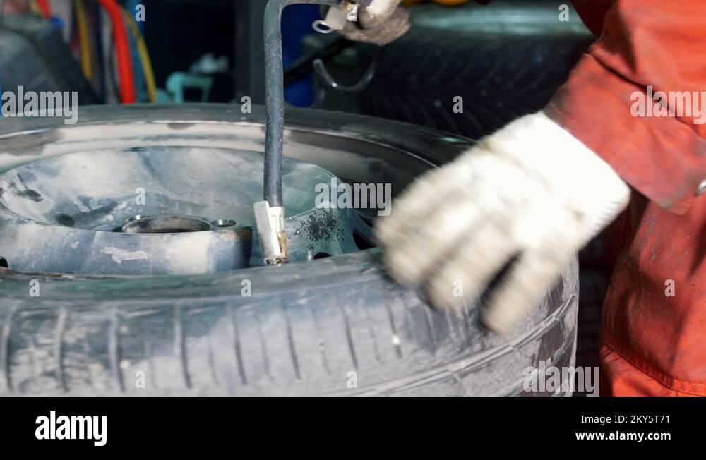 Worker in car service inflates tyres with air - mechanical workshop ...
