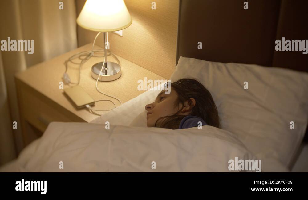 Cute little girl in her room at night, lying on the bed. she turns off ...