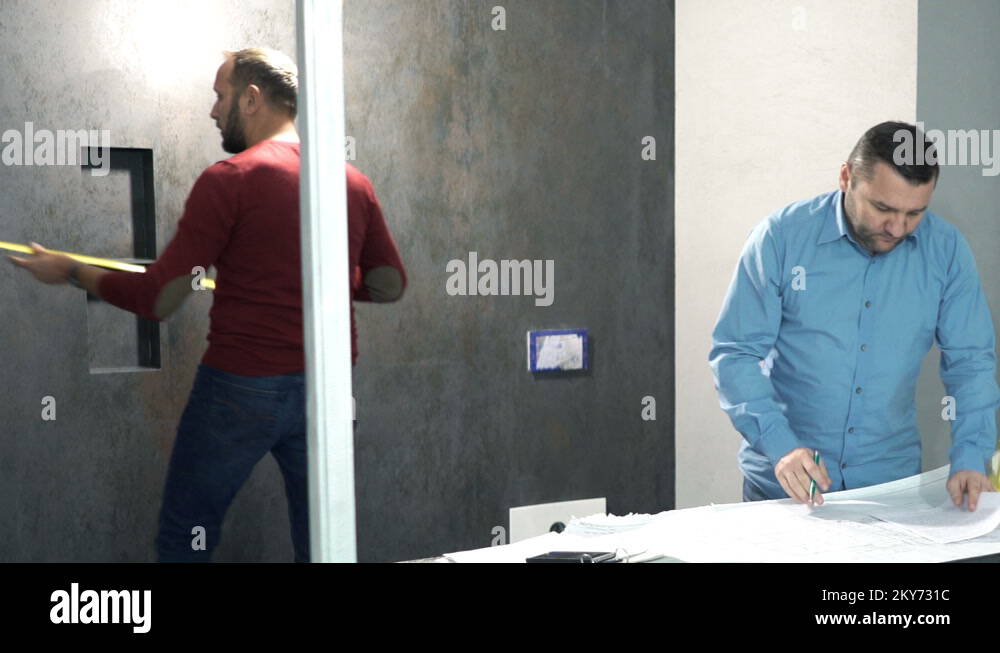 Two male architects with blueprints measuring wall at new home Stock ...