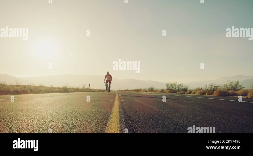 Slow motion man cycling on road bike outside on desert road with lens ...