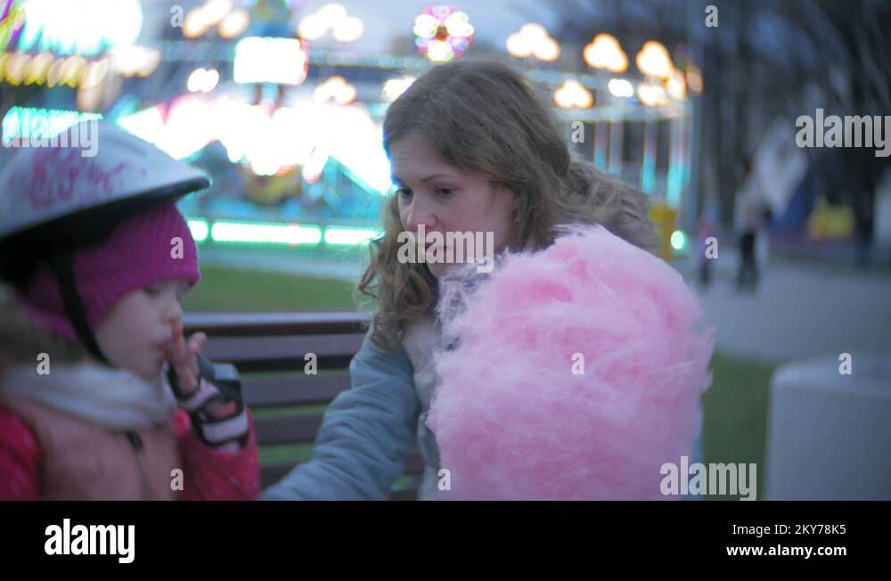 Beautiful little girl sitting on a bench in an amusement park, eating ...