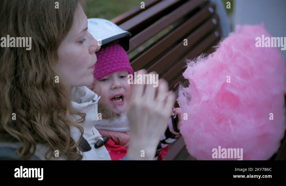 Beautiful little girl sitting on a bench in an amusement park, eating ...