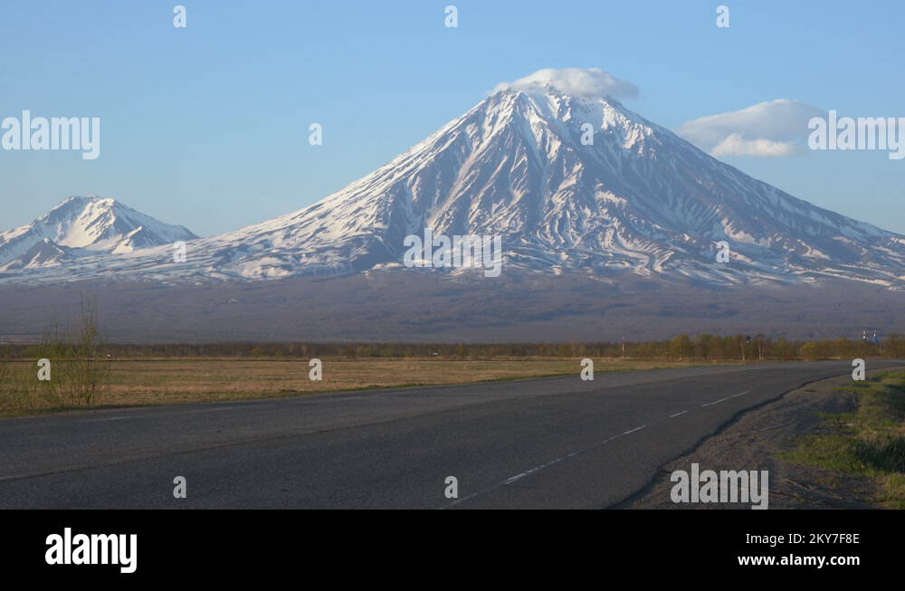 Cars drive along an asphalt highway on background of active volcano ...