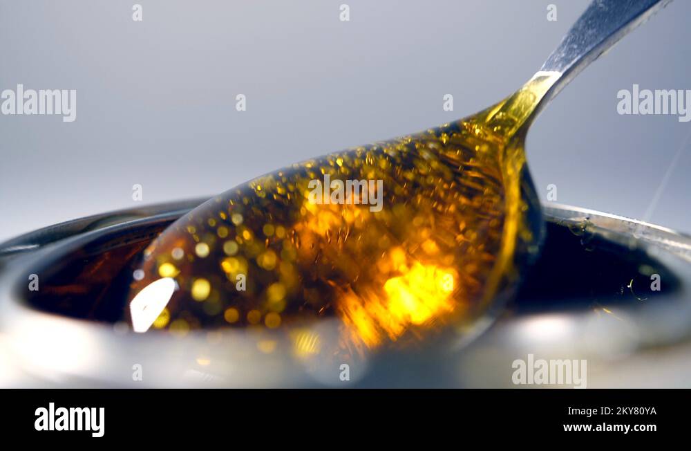 golden syrup dripping from a spoon into a metal container, honey ...