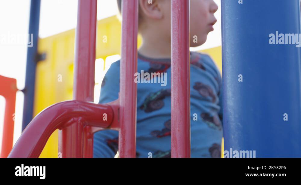 Toddler boy grabs onto bars on play structure at park - sun flare Stock ...