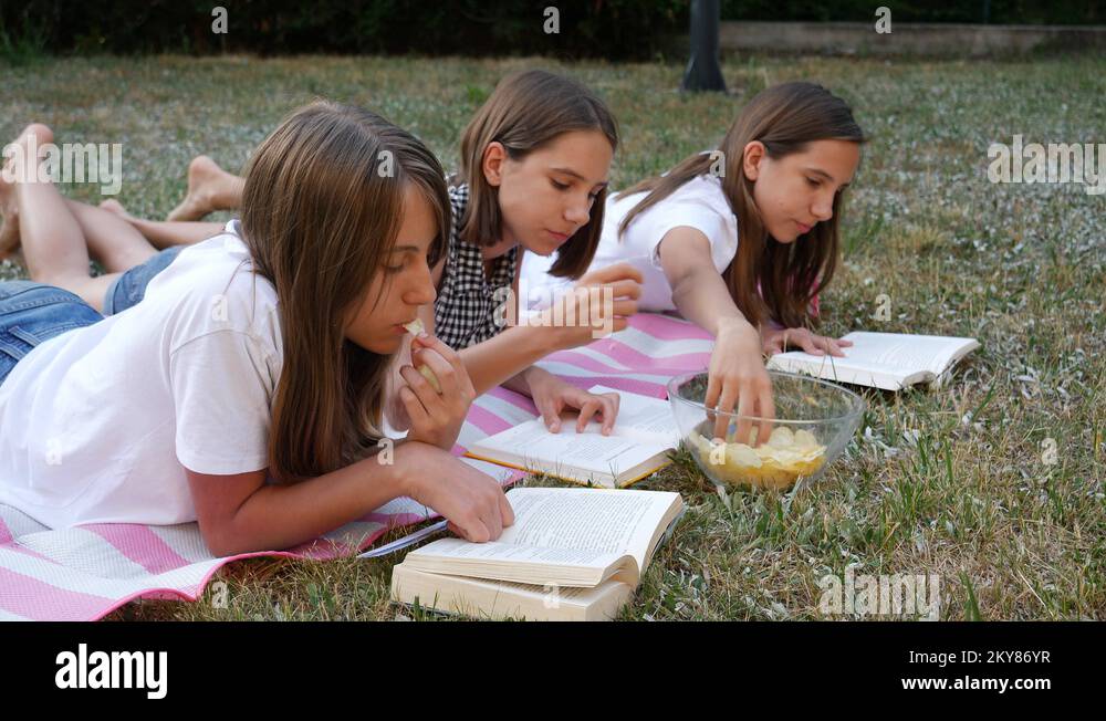 Slow motion teen girls sisters lie on backyard rug read books eat ...