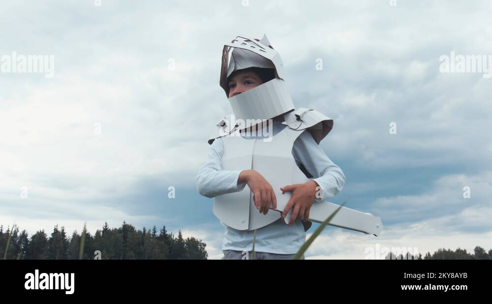 Kid boy wearing cardboard medieval knight armor costume draws a sword ...