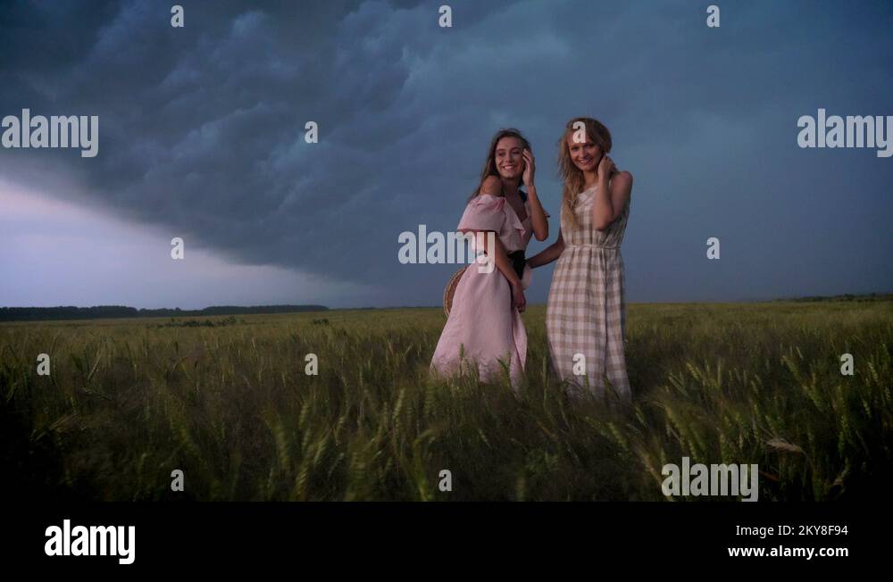 Two young charming girls in dresses is enjoing wind in field in rainy ...