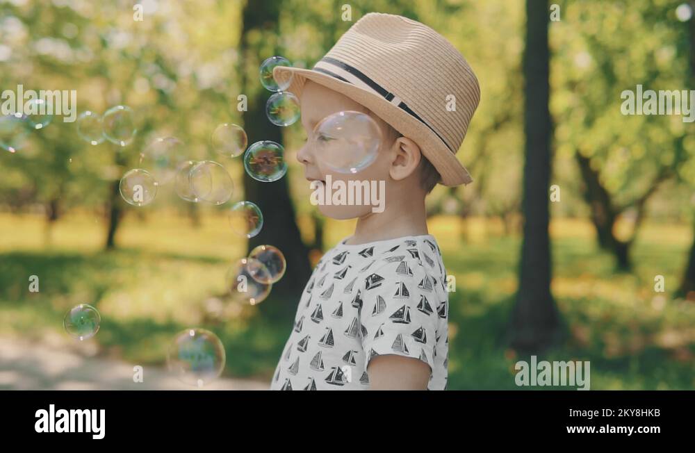 Little boy in hat catching bubbles. Little child playing with parents ...