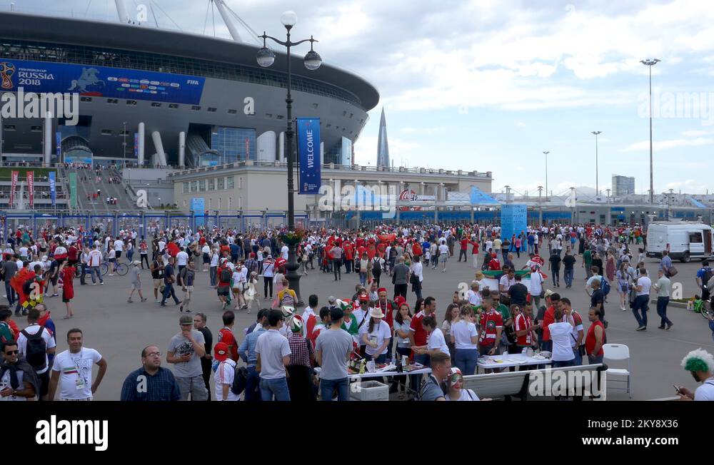 Right to left pan football fans behind stadium entrance gates with flag ...