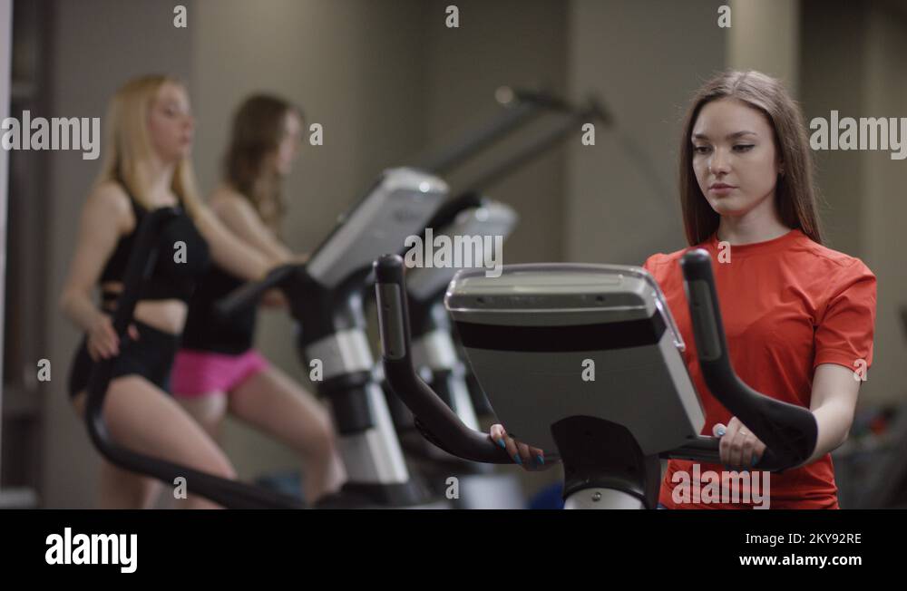 cute girl is diligently working on an exercise bike and cool guy come ...