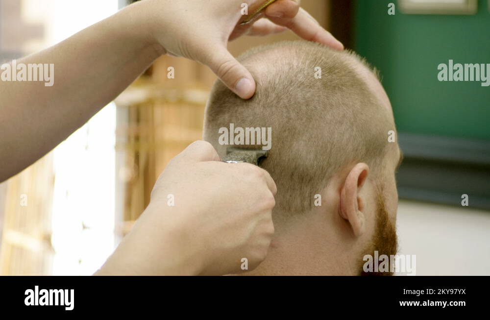 Barber making haircut for young redhead man with a beard in a barber's ...
