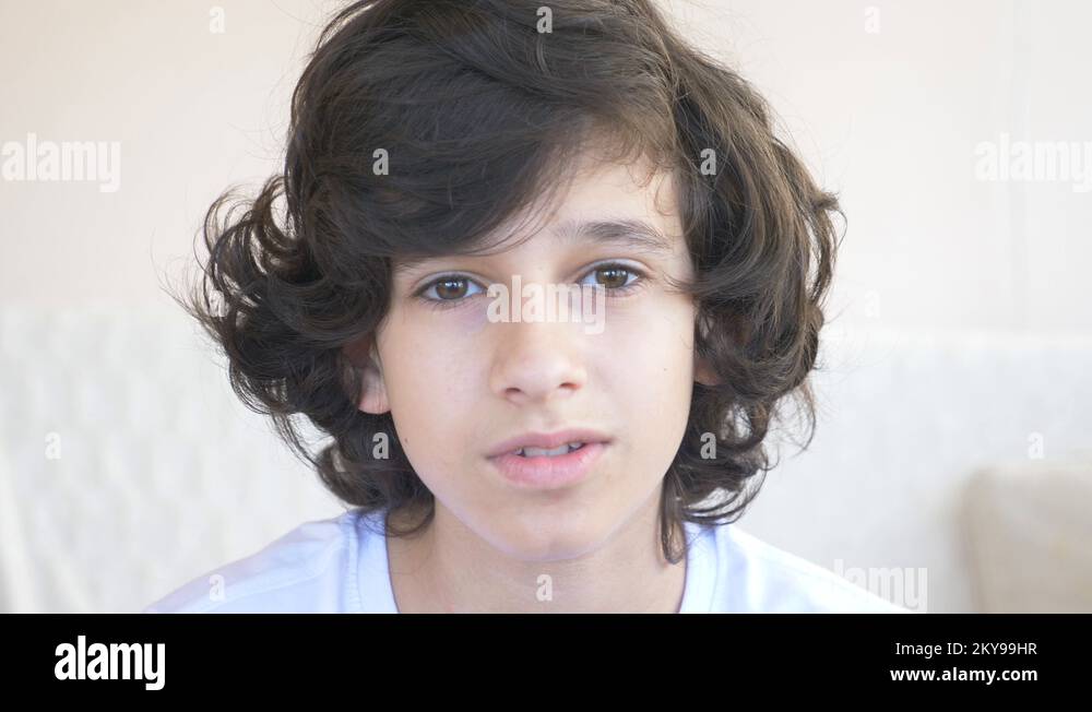 cute curly-haired boy teen looking into camera and making funny face ...