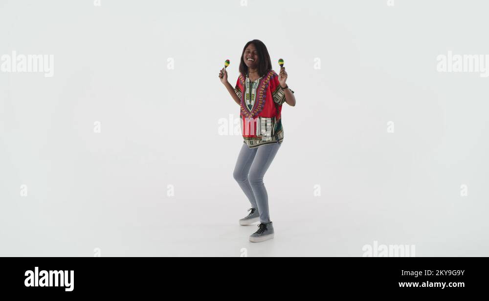 Full-height shot beautiful African teenager shaking maracas and jumping ...