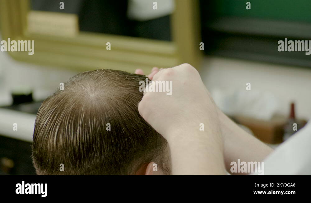 Barber making haircut for young blond man with a beard in a barber's ...