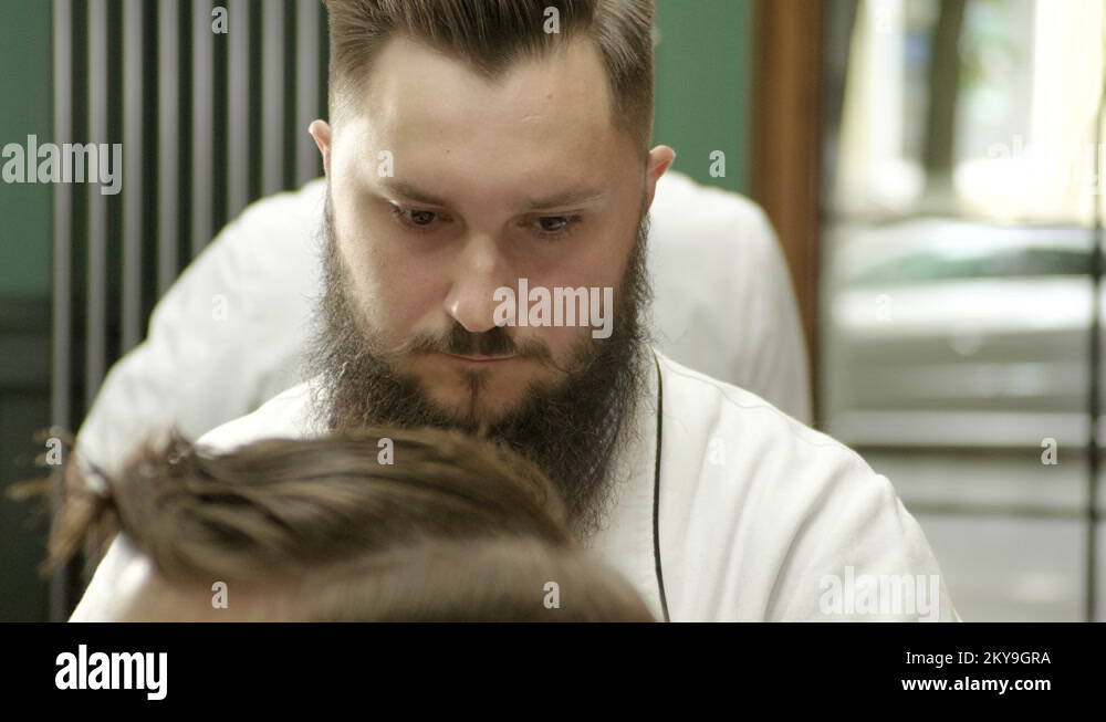 Barber making haircut for young blond man with a beard in a barber's ...