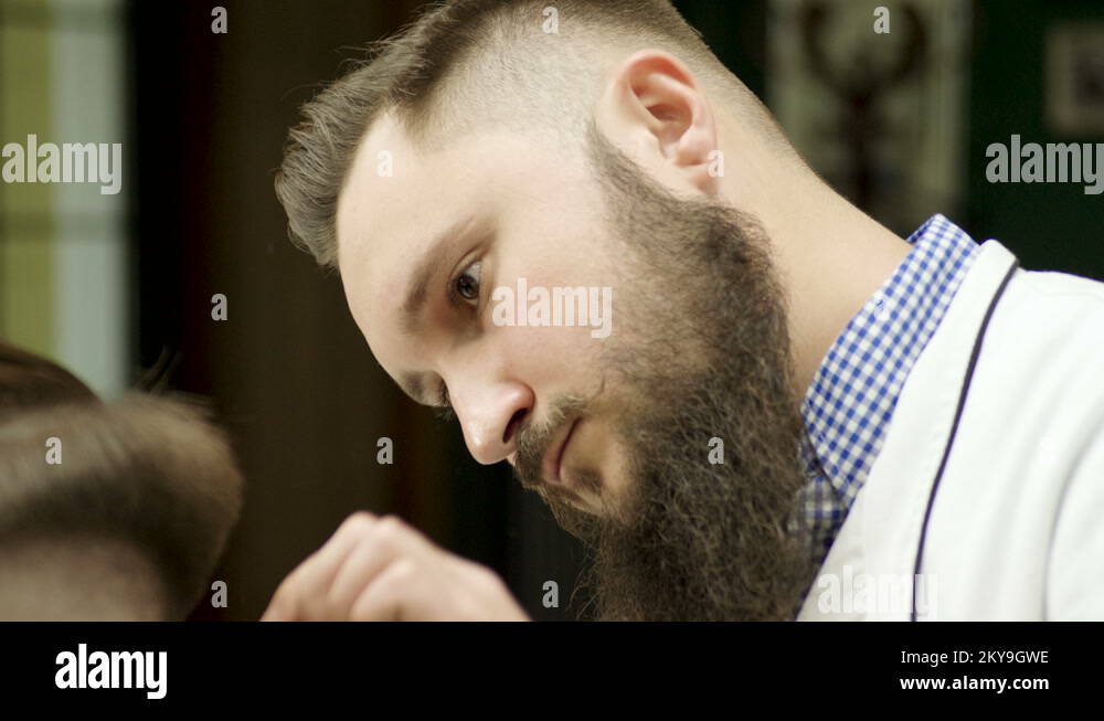 Barber making haircut for young blond man with a beard in a barber's ...