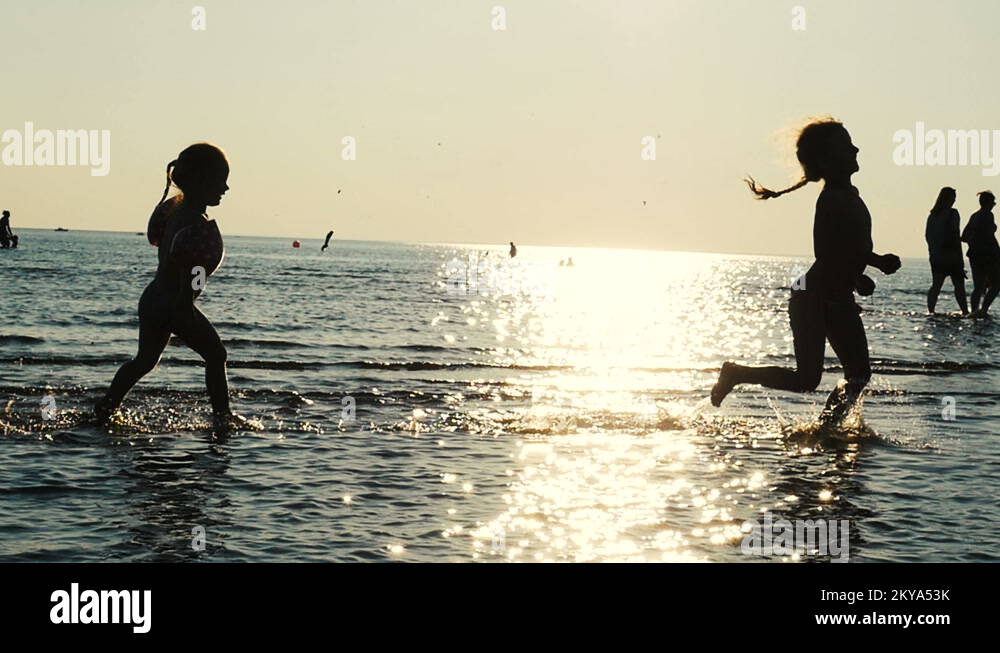 Children playing in the sea water in sun flare, kids silhouette playing ...